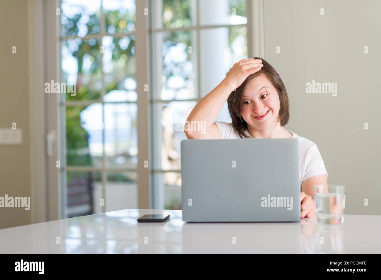 Down syndrome woman at home using computer laptop stressed with hand on ...