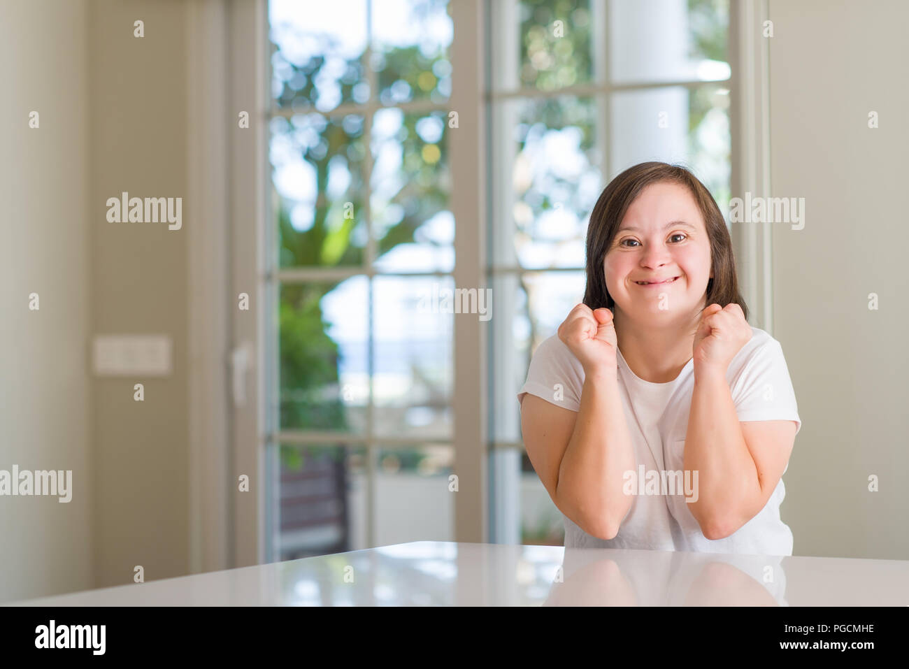 Down syndrome woman at home excited for success with arms raised ...