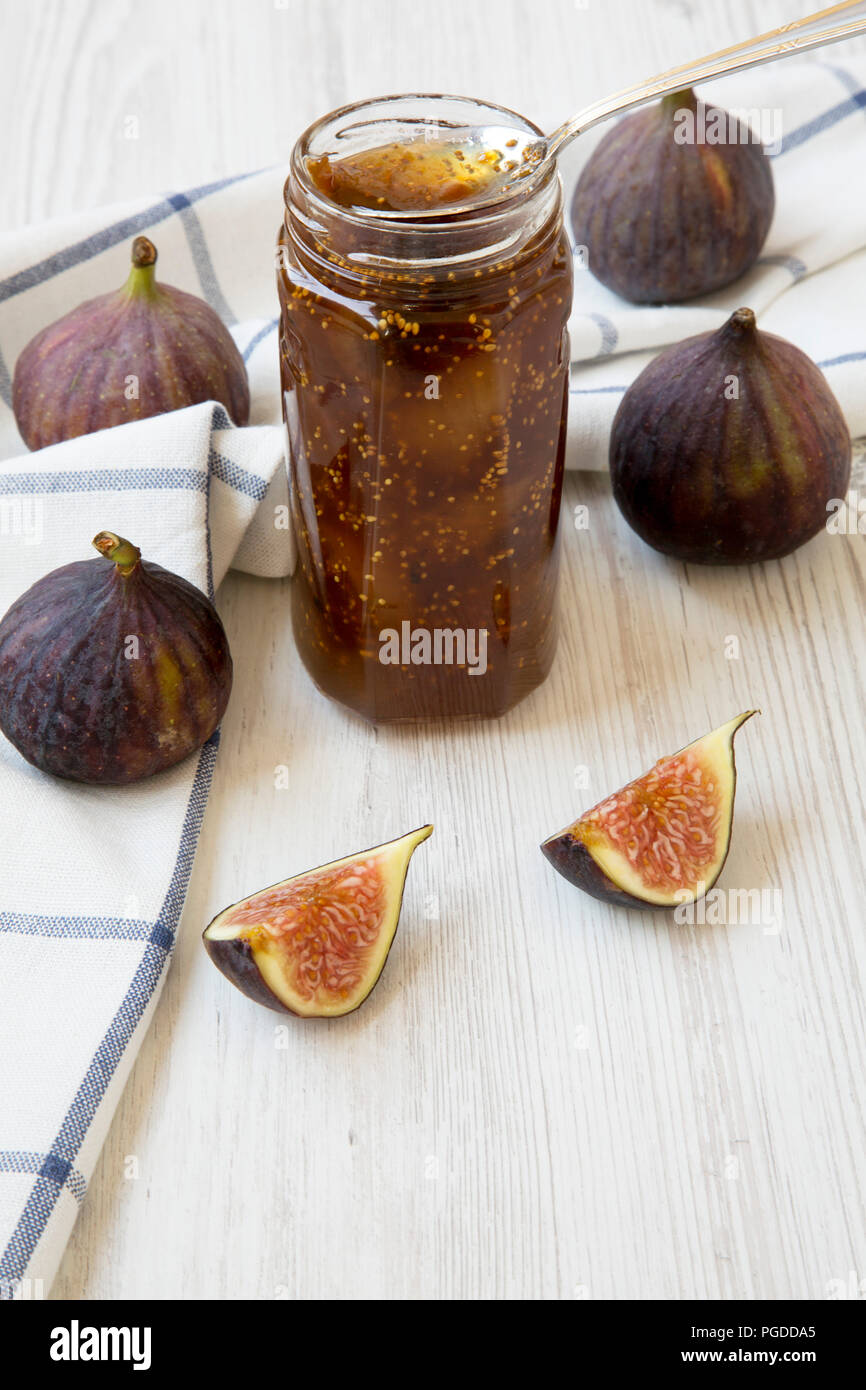 Fig jam in glass jar and fresh figs on white wooden table, side view ...