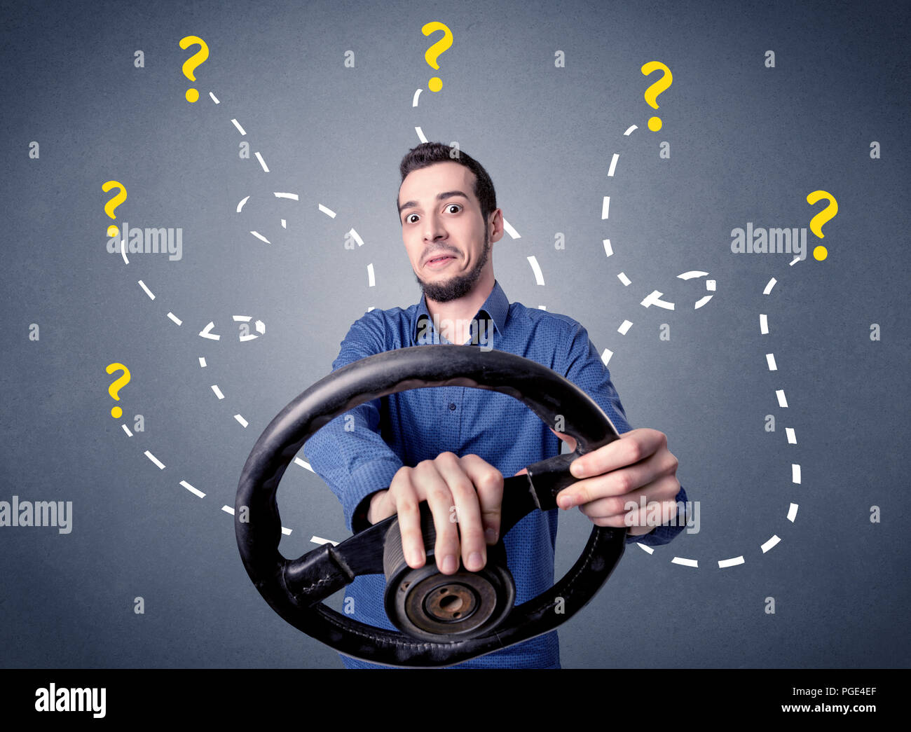 Young man holding black steering wheel with question marks around him ...