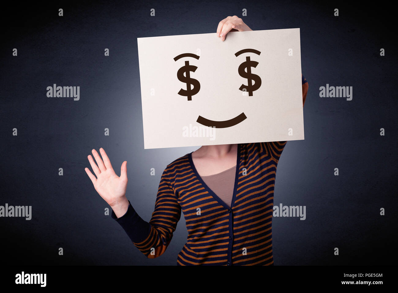 Young casual woman hiding behind a greedy face drawing on cardboard ...