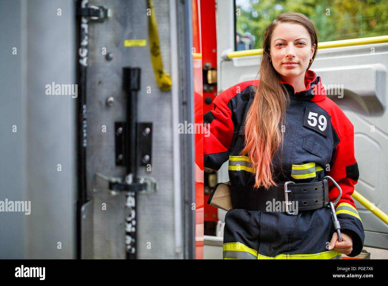 Photo of fire woman with long hair in overalls stands in fire engine ...