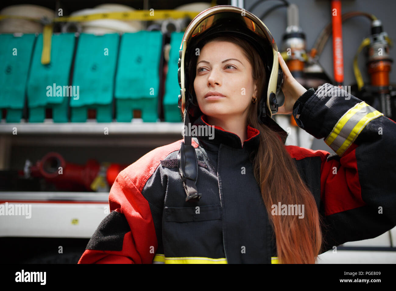Photo of young fire woman with long hair in helmet next to fire engine ...