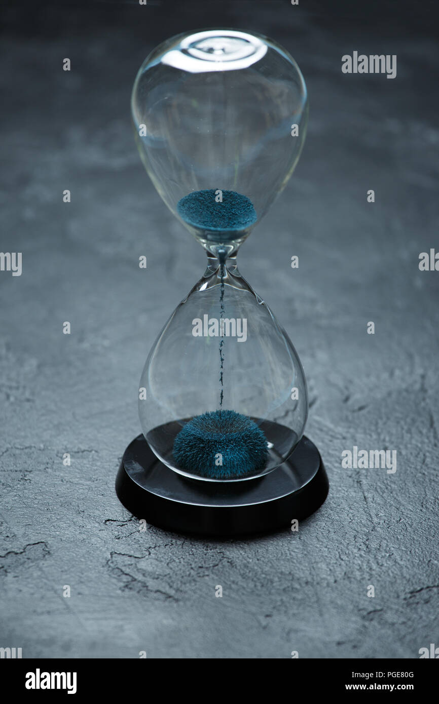 Image of hourglass with blue sand on black background Stock Photo - Alamy