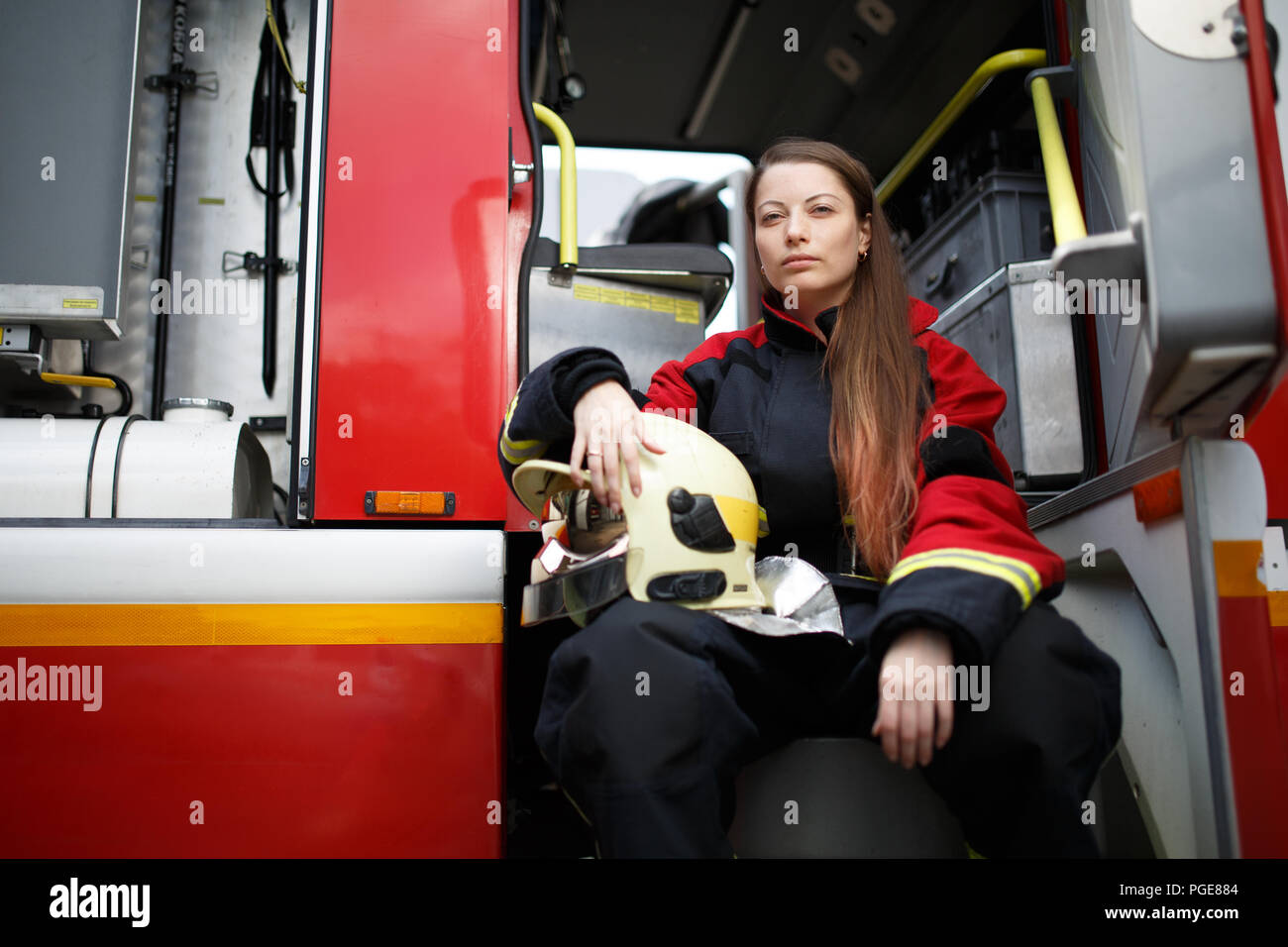 Photo of young fire woman with long hair in overalls sits in fire truck ...