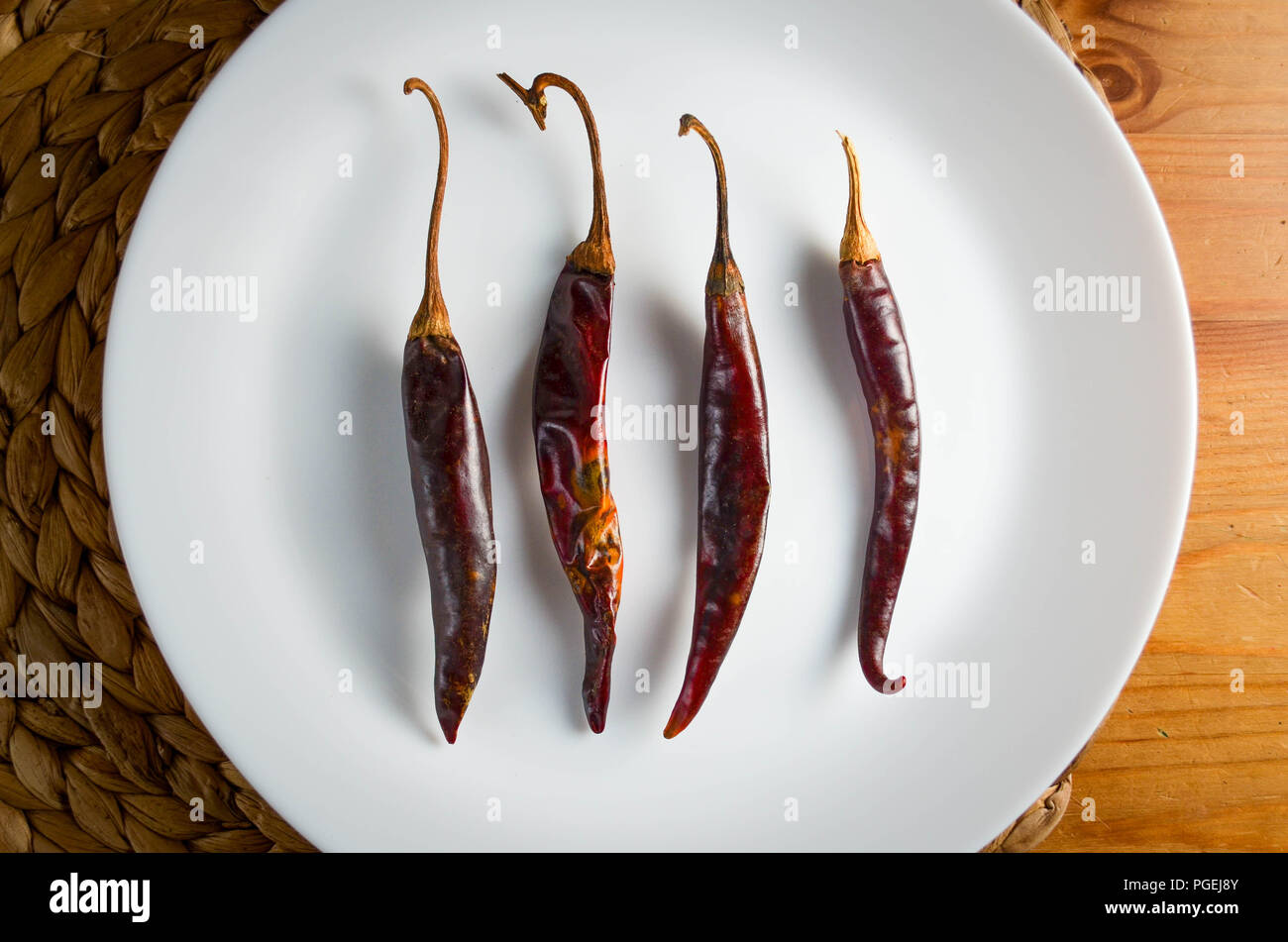 Four puya chilies on a white plate against a pine wood and woven ...