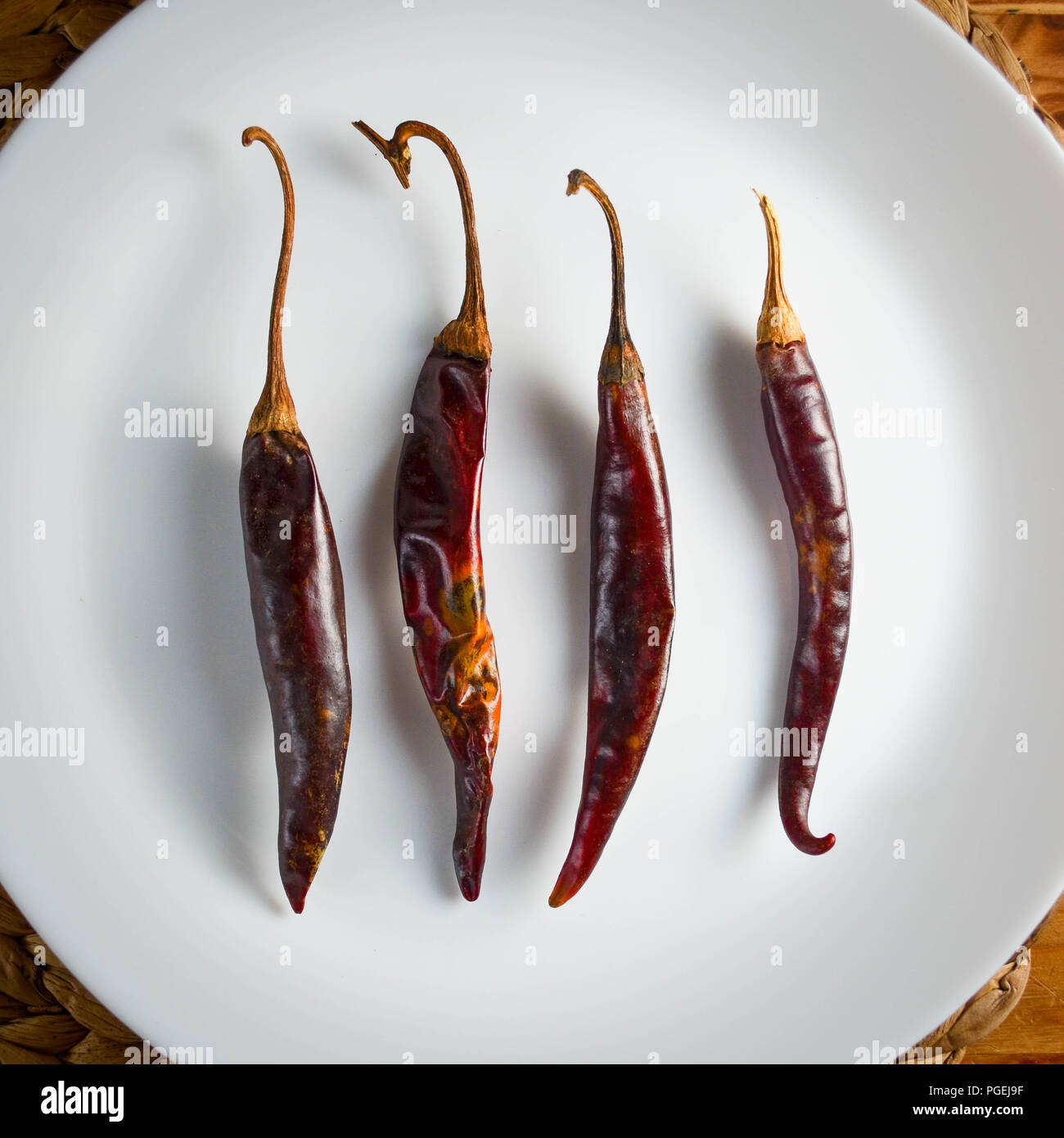 Four puya chilies on a white plate against a pine wood and woven ...