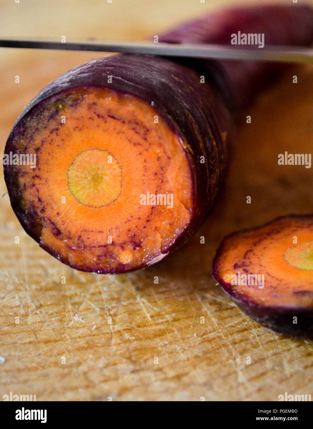 A purple carrot with the end cut off, showing the orange interior. The ...