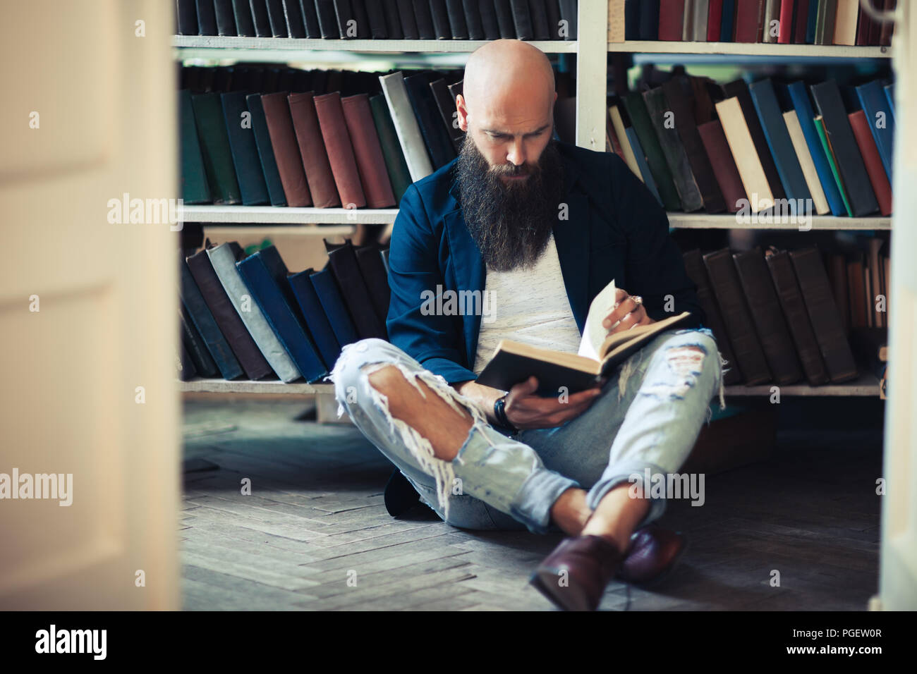Handsome bearded man sitting on floor, reading book and relaxing in ...