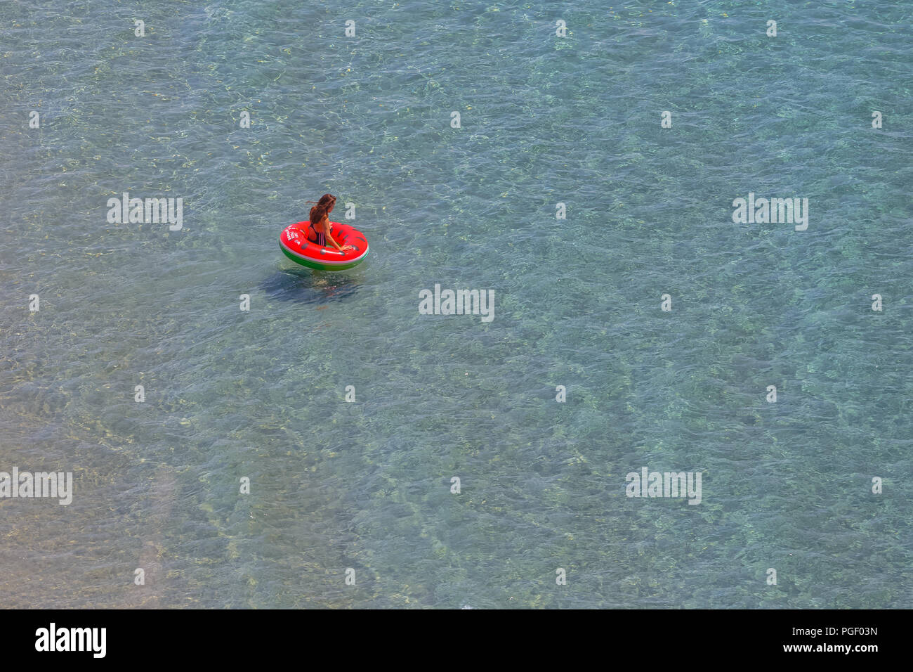 Beautiful girl having fun in a red melon shaped buoy floating onto the ...