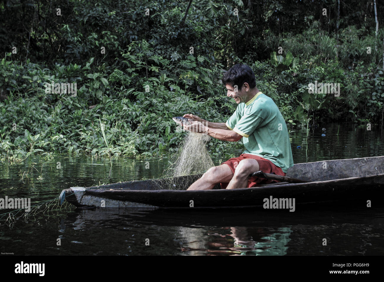 Fisherman in dugout canoe checks his fishing net in the Amazon rain ...