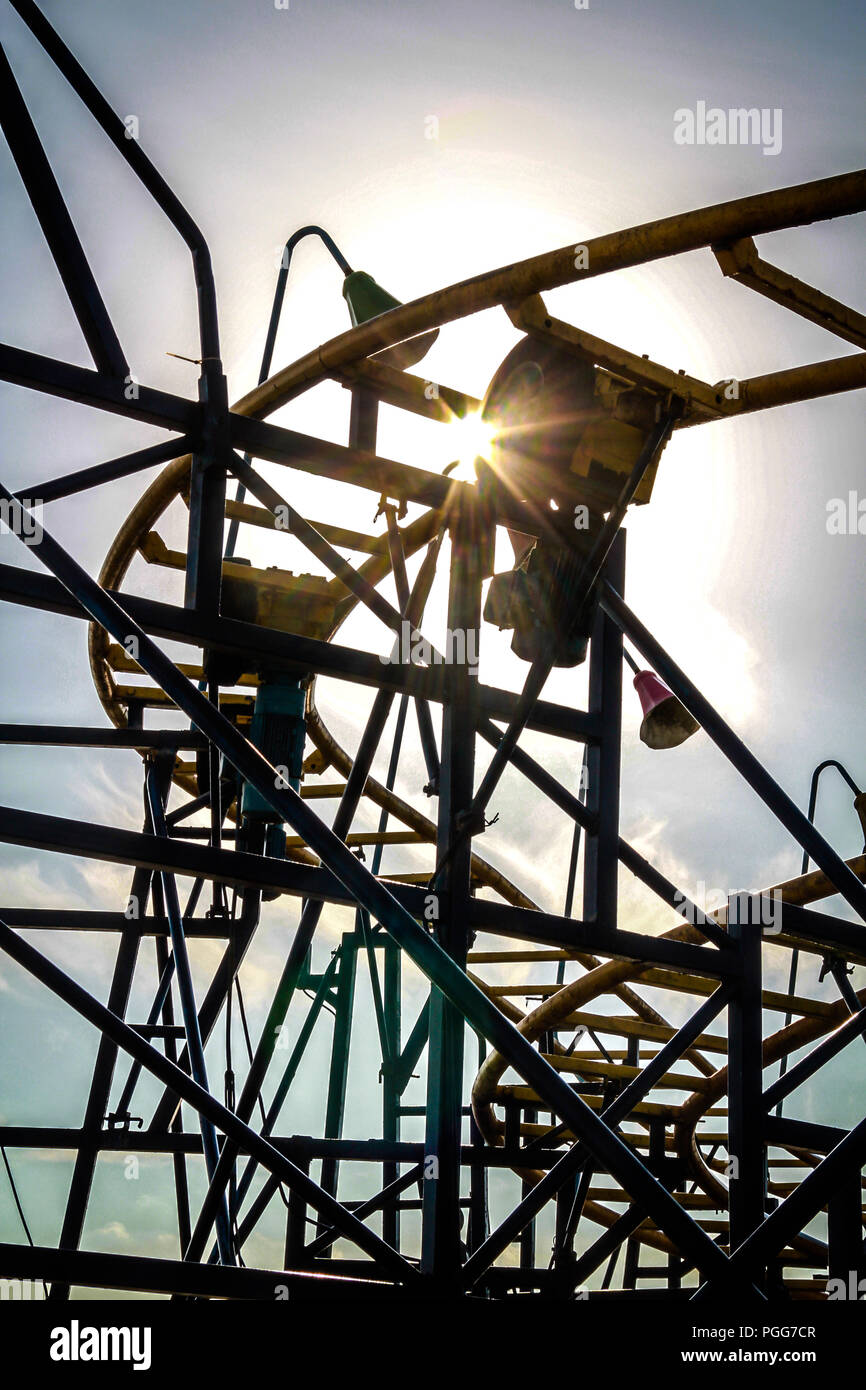 A silhouette shot of a roller coaster track. Behind it is the sun ...