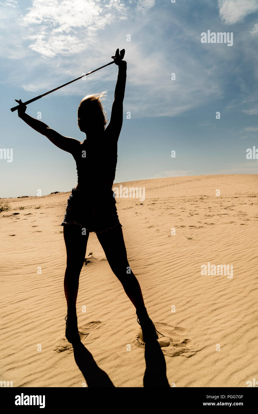 Silhouette of a woman with flying hair with golf putter in the desert ...
