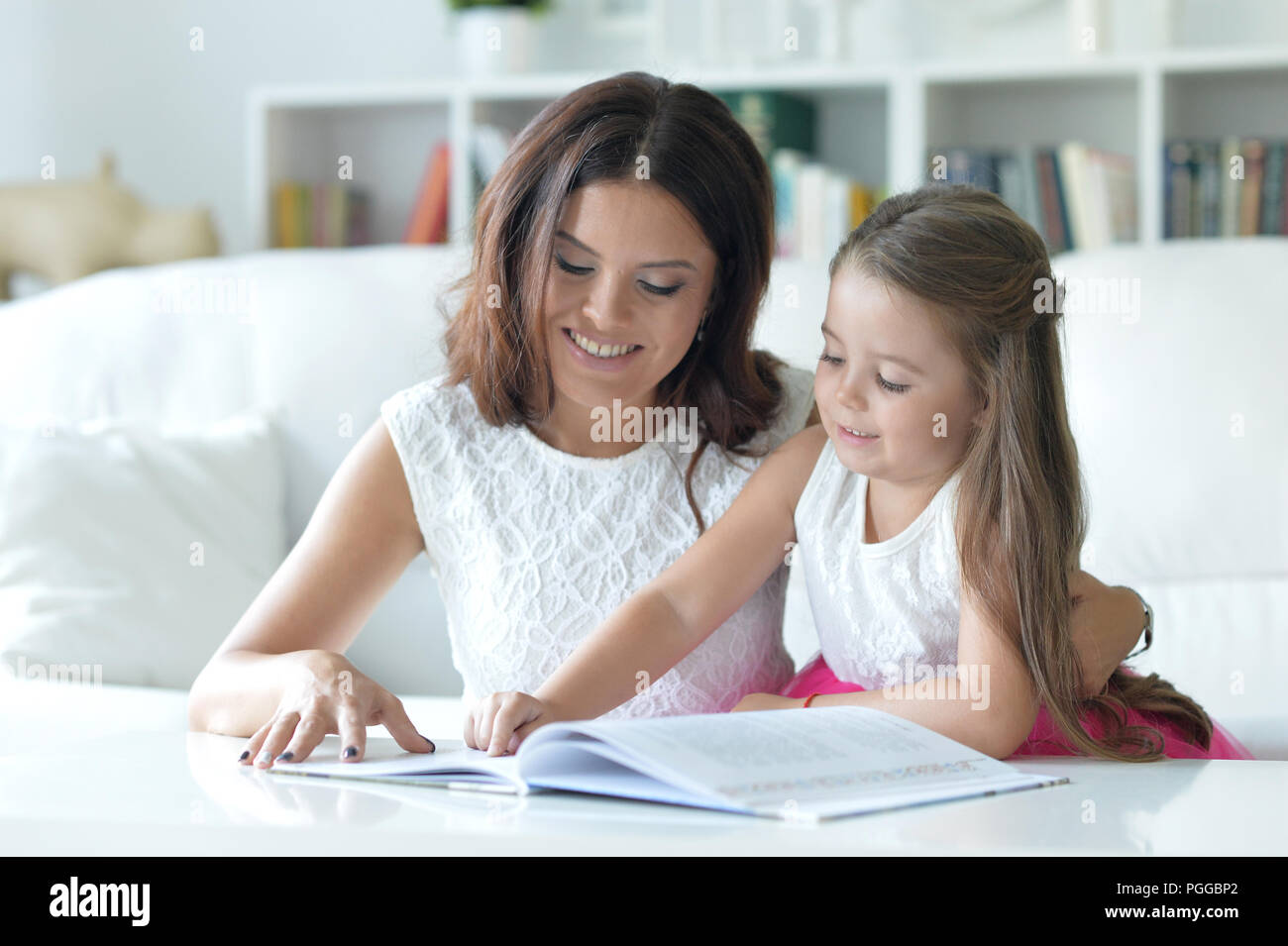 little cute girl reading book with mother at the table Stock Photo - Alamy
