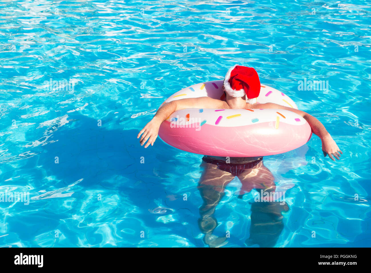 top view of young drunk guy in christmas hat swim with pink circle in ...