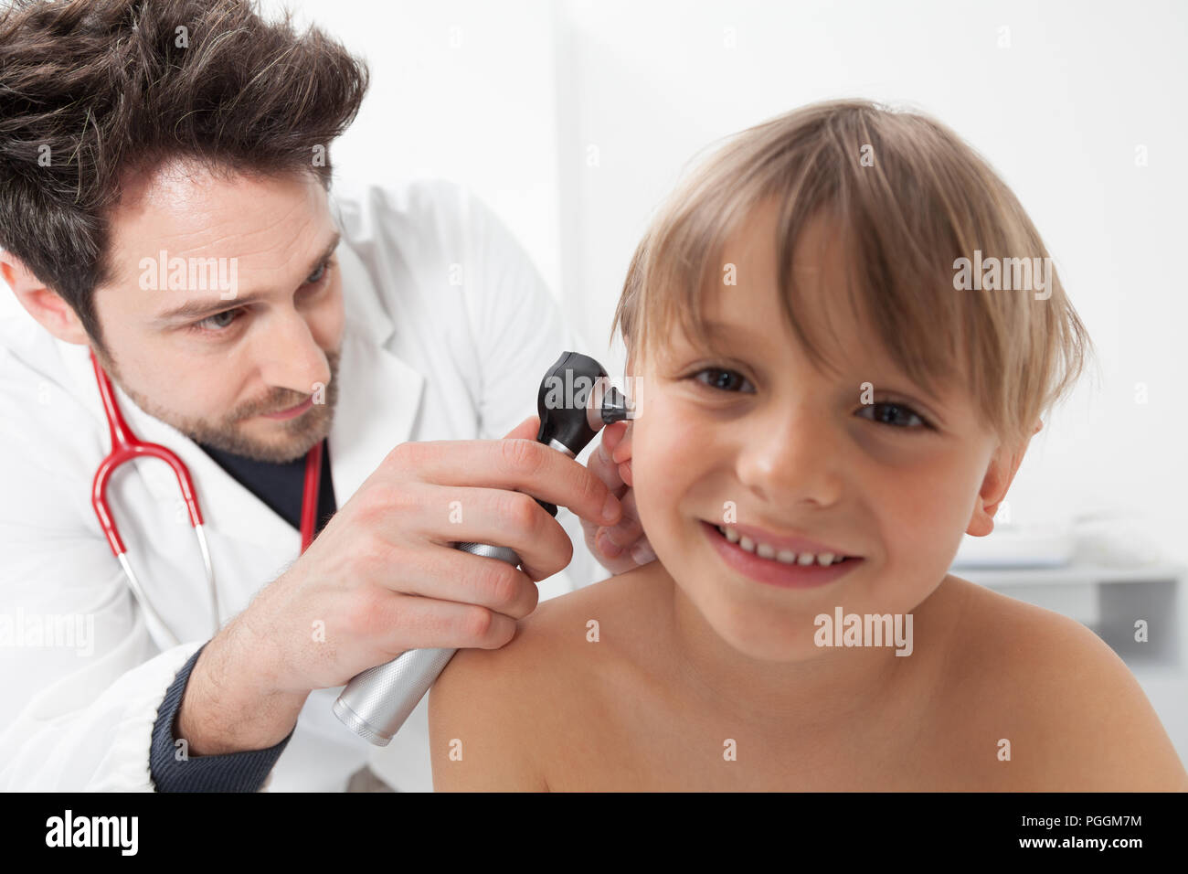 A pediatric doctor with an otoscope doing a ear exam with a blond hair ...