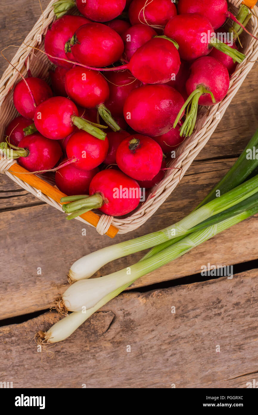 Fresh radishes in basket in green onion. Top view. Wooden desk table ...