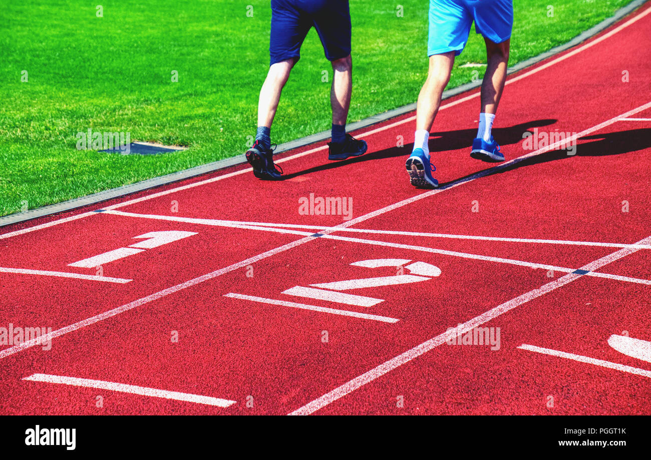 Male athletes are running on outdoor stadium track. Red rubber running ...