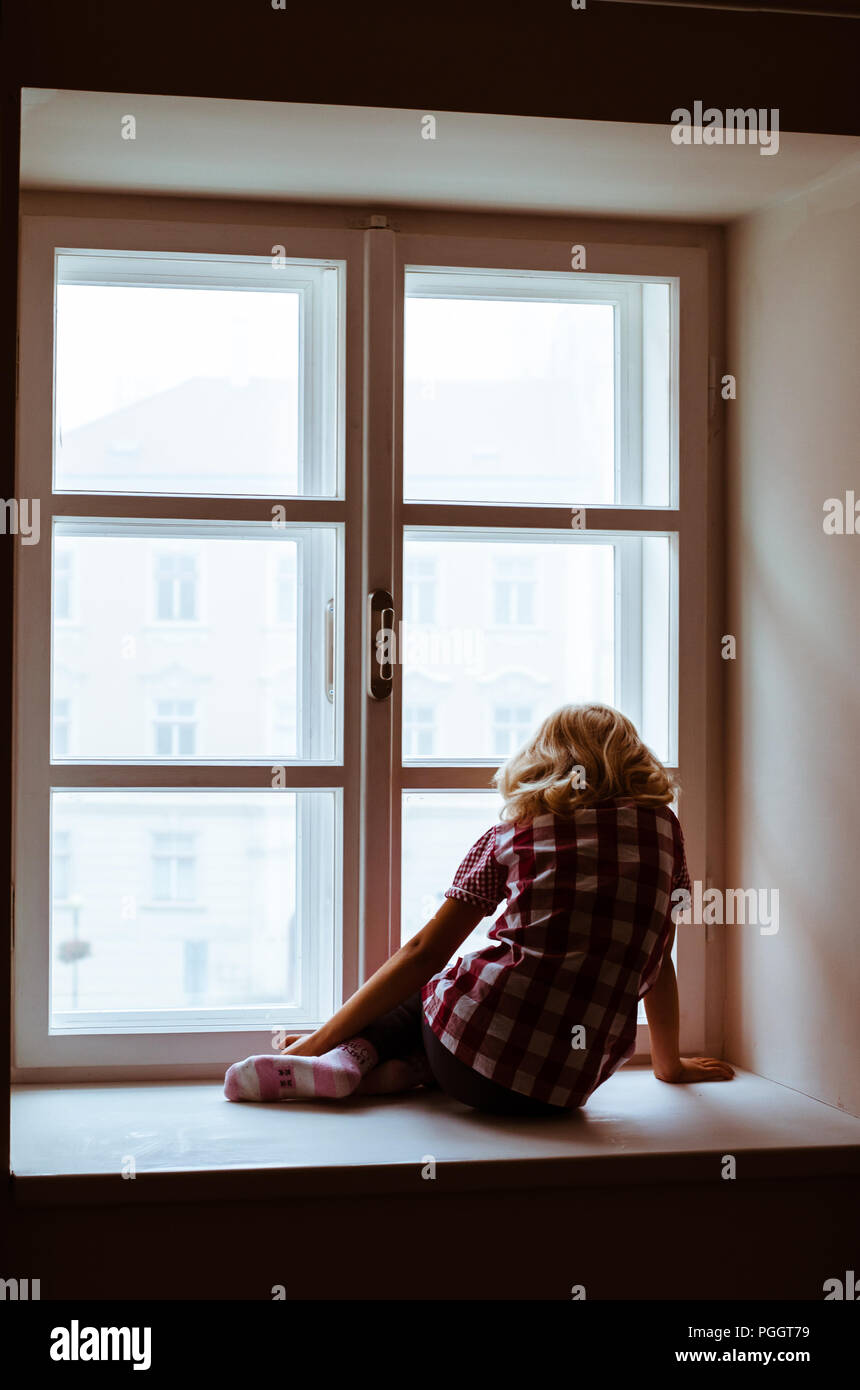 little blond girl sitting and looking over window Stock Photo - Alamy
