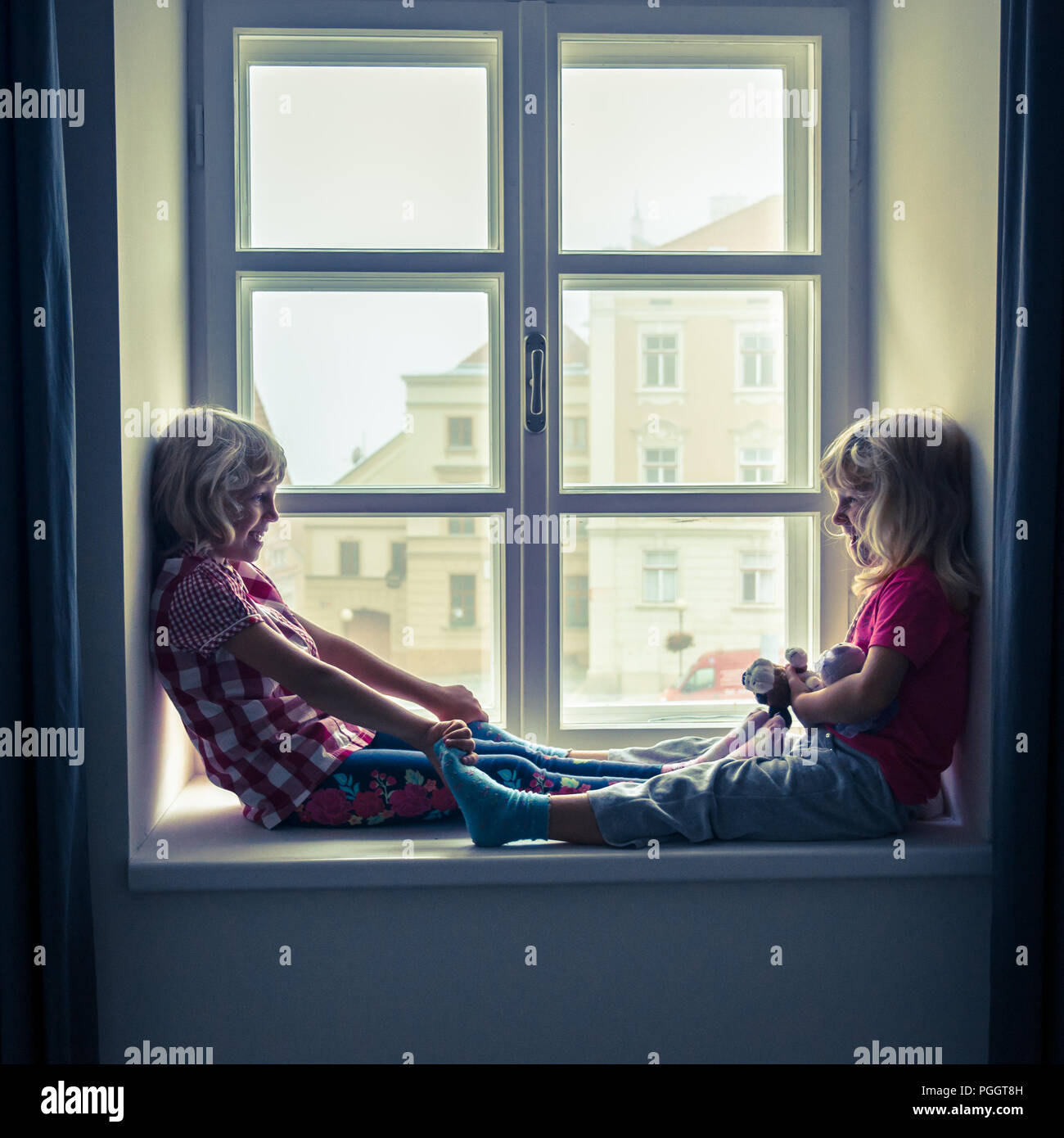 two happy girls sitting on the window playing Stock Photo - Alamy