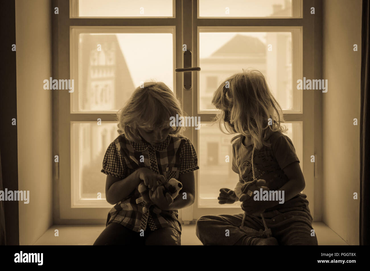 two happy girls sitting on the window playing Stock Photo - Alamy