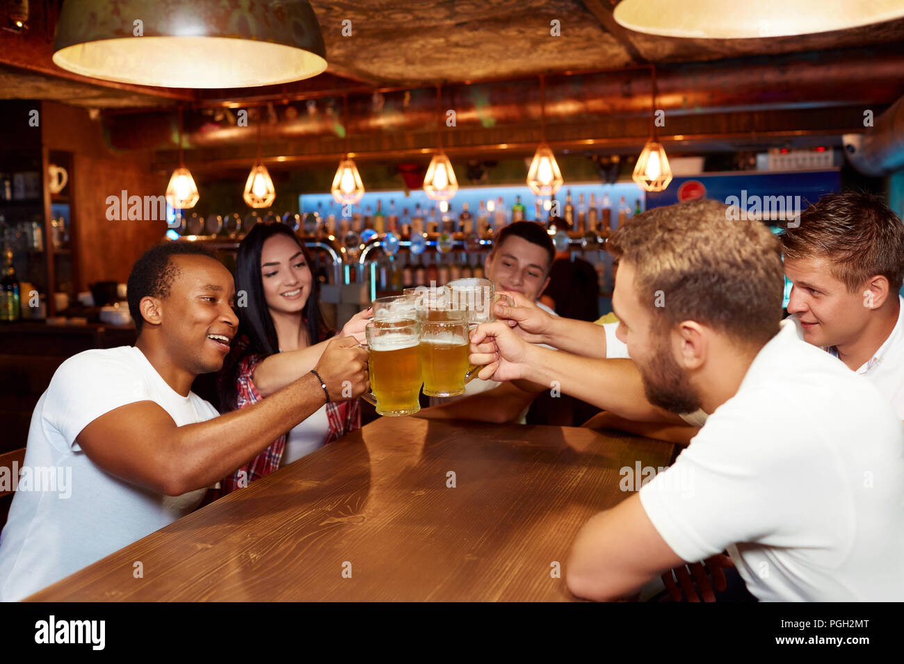 Group of happy friends enjoying beer at design pub, toasting and ...