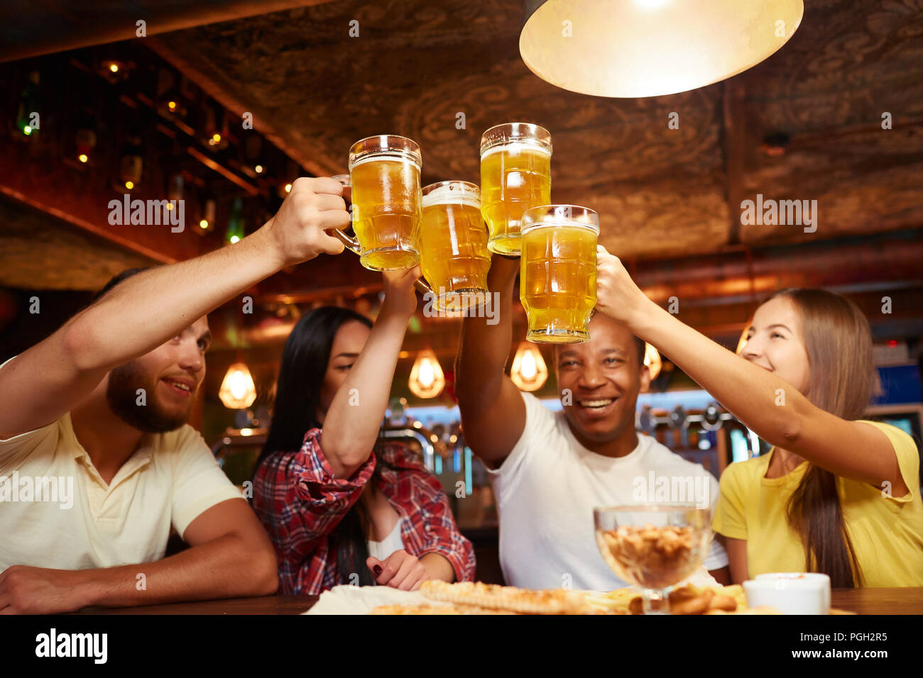 People raising beer glasses high above table and looking on drink ...