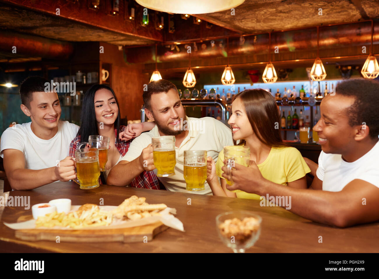Company of happy friends sitting in bar at table with beer and snacks ...