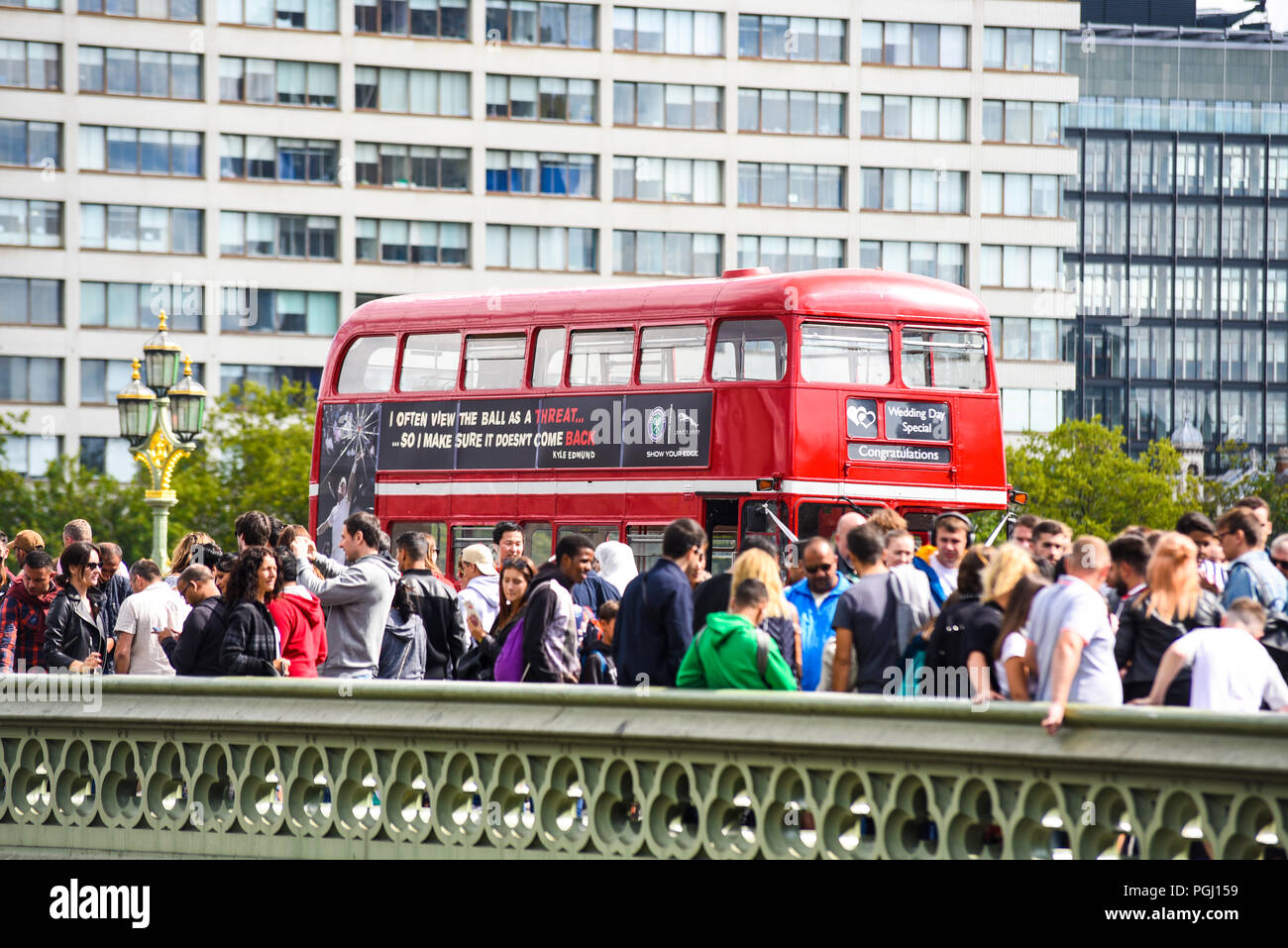 Red London bus and large numbers of people crossing Westminster Bridge ...