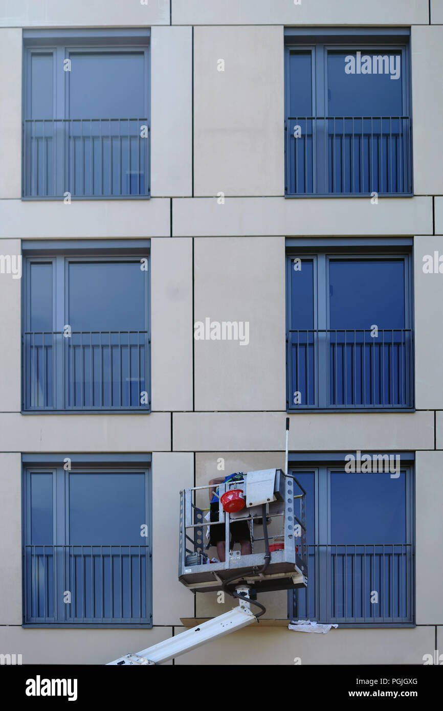 A window cleaner stands on a lift and cleans the windows of a ...