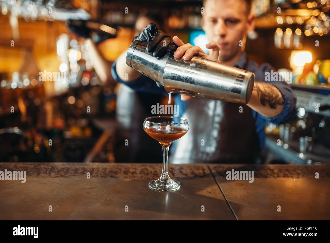 Male bartender pouring the drink from the shaker at the bar counter ...