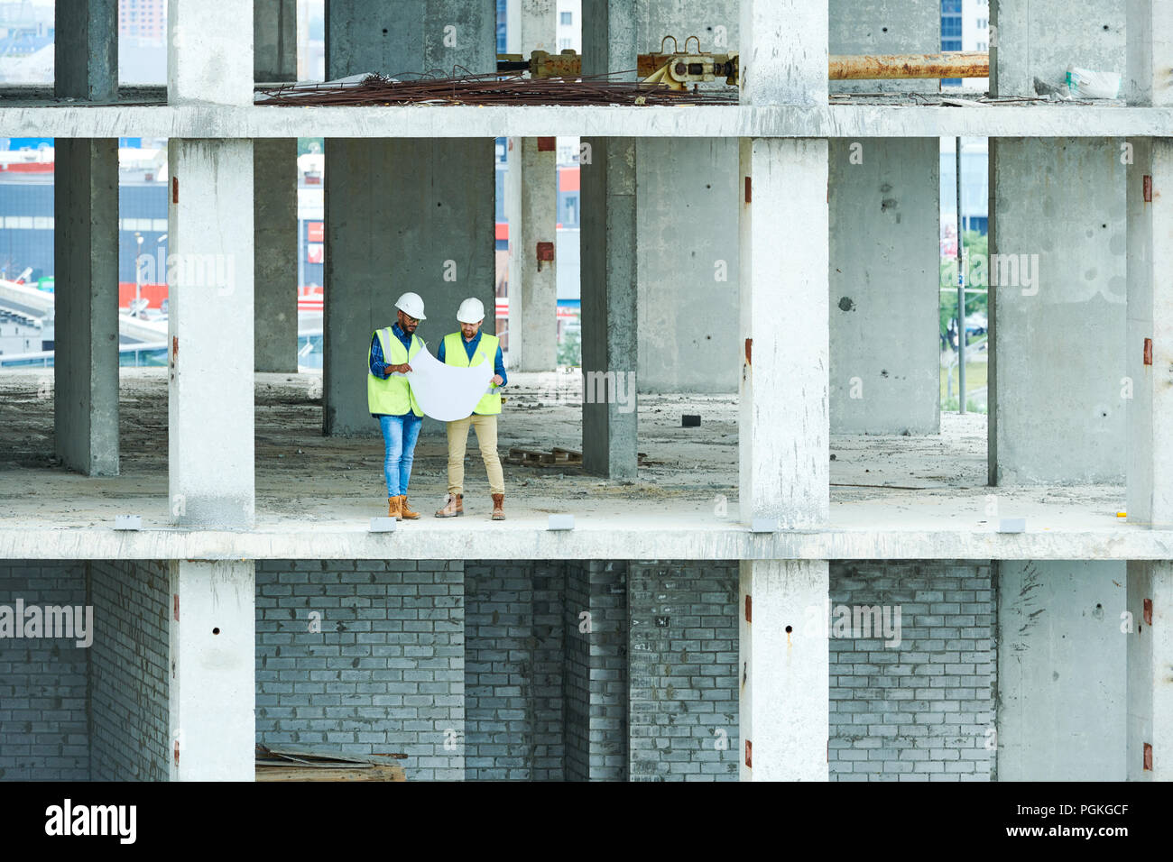 Wide angle view at two builders holding plans standing in unfinished ...