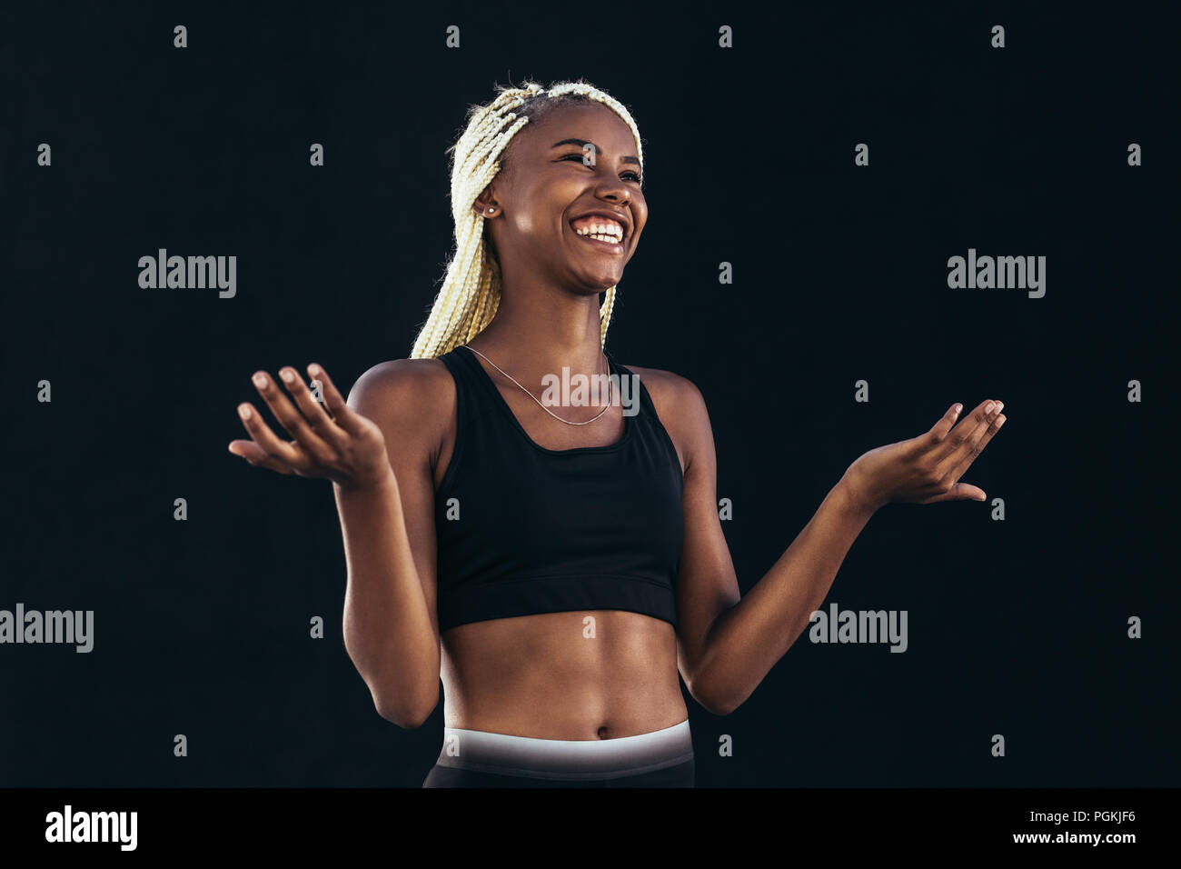 Happy female sprinter standing against black background with open hands ...