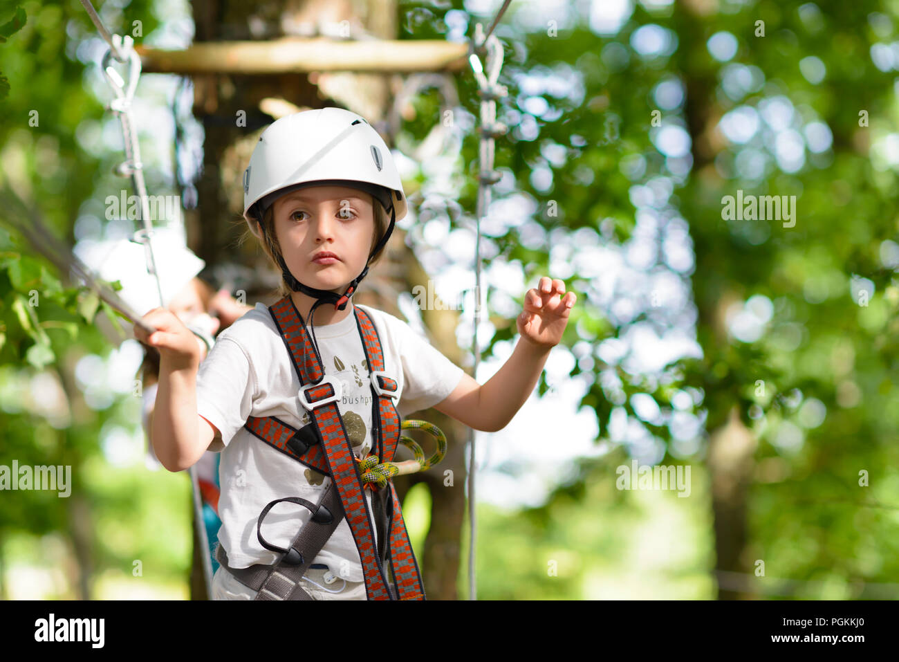 Happy kid climbing on high wire in a adventure park Stock Photo - Alamy
