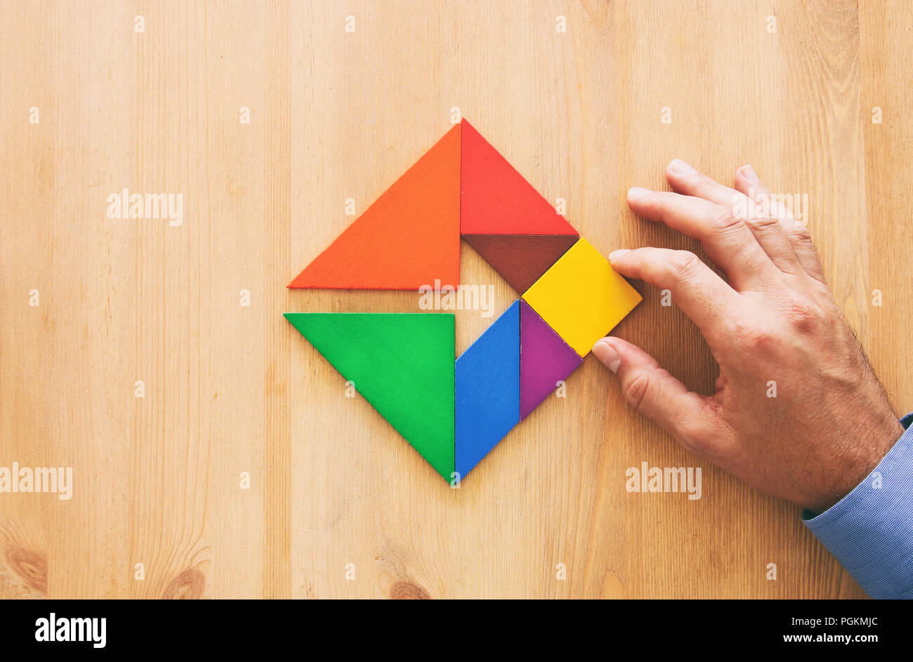 man's hand holding a missing piece in a square tangram puzzle, over ...
