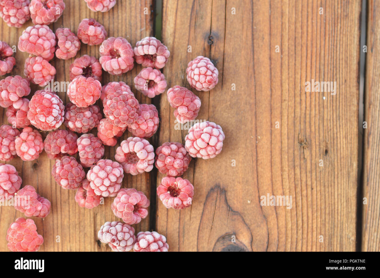 Frozen raspberry berries are lying on a wooden background on the left ...