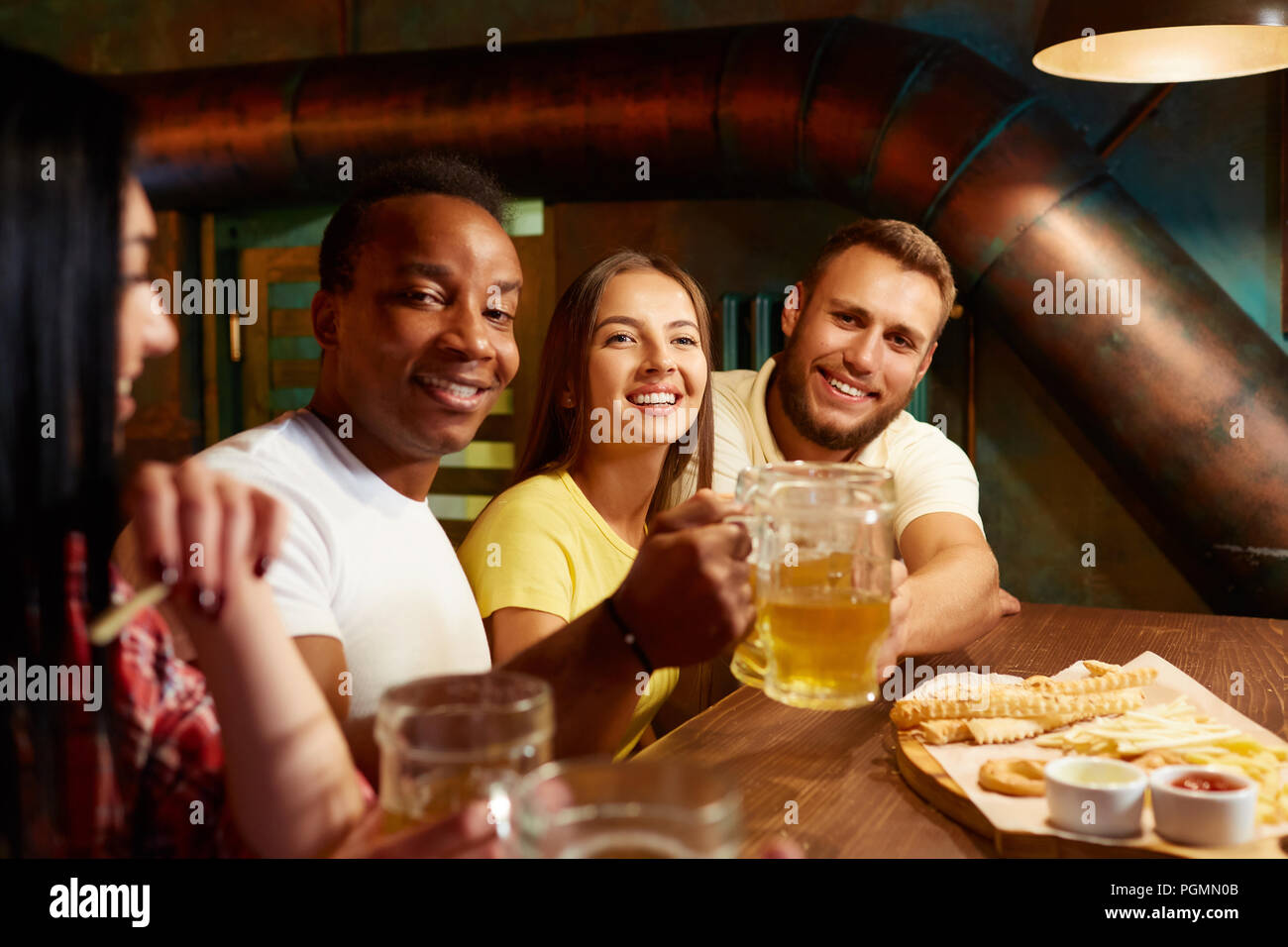 Company of happy friends sitting in bar at table with beer and snacks ...