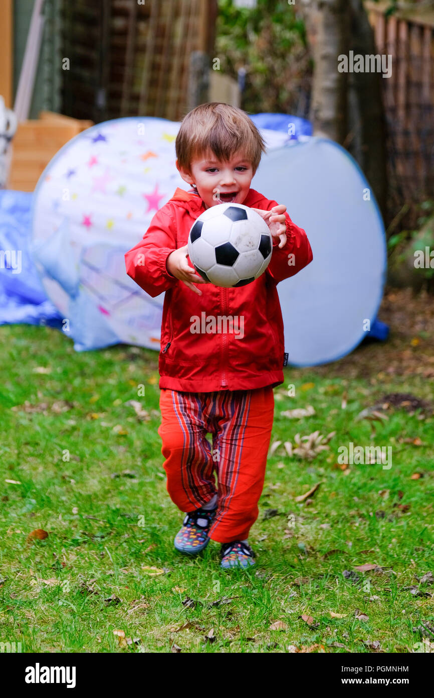 Boy aged two (2) with red coat and football happy and smiling as he ...