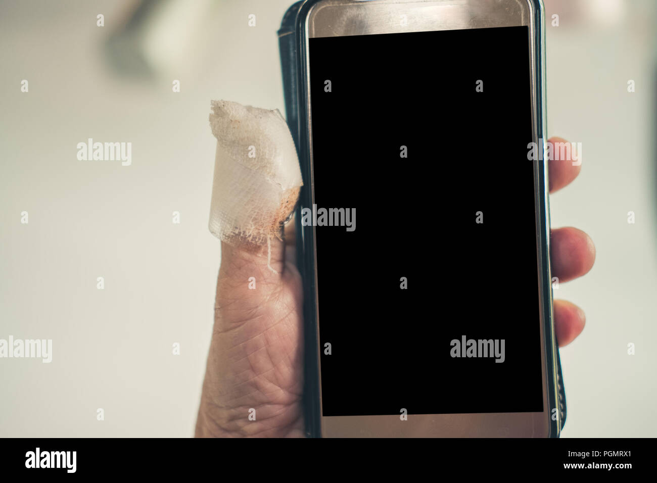 injured hand holding mobile phone with white adhesive bandage on thumb ...