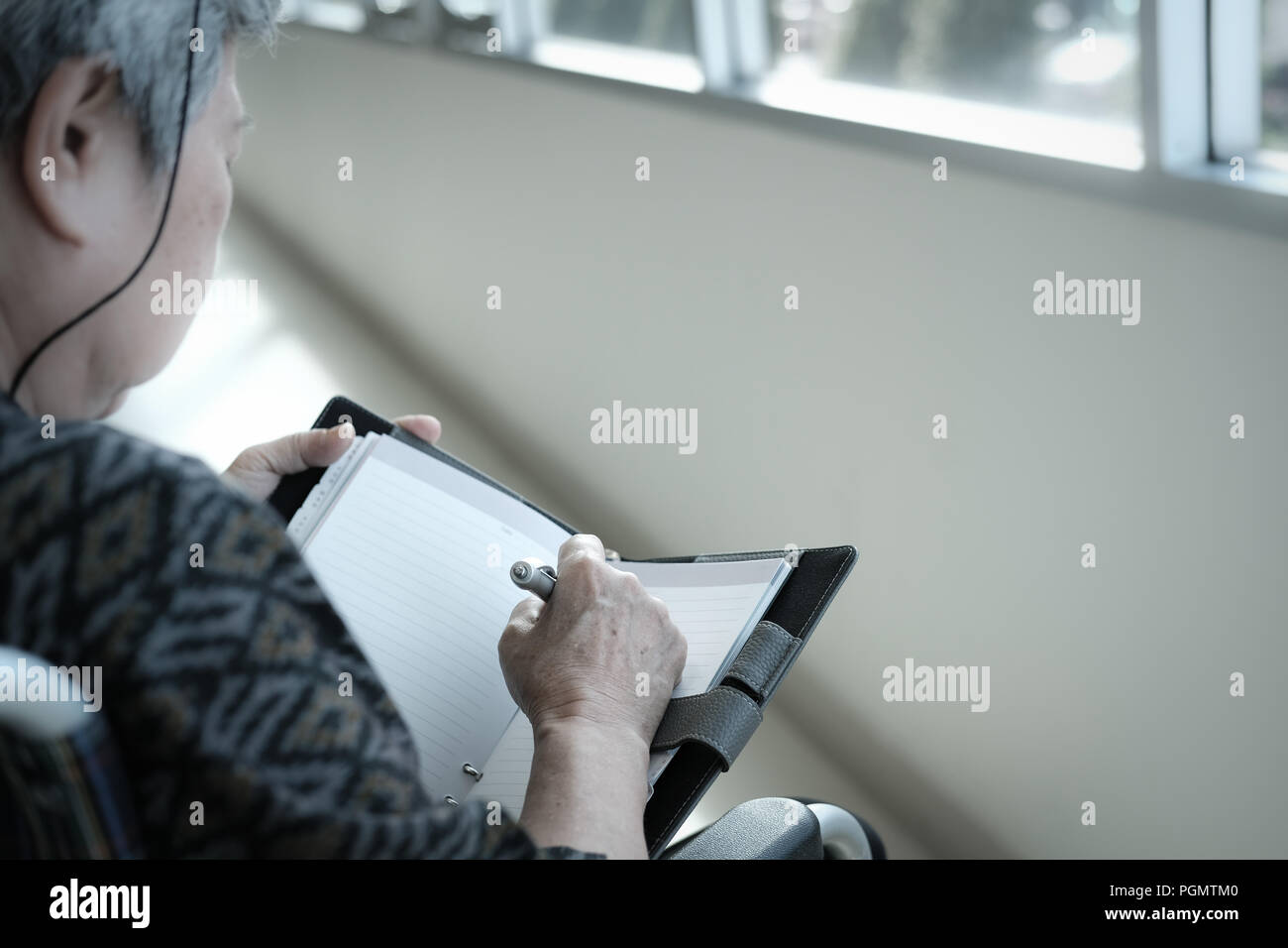 elder woman in wheelchair writing note on notebook near window. elderly ...