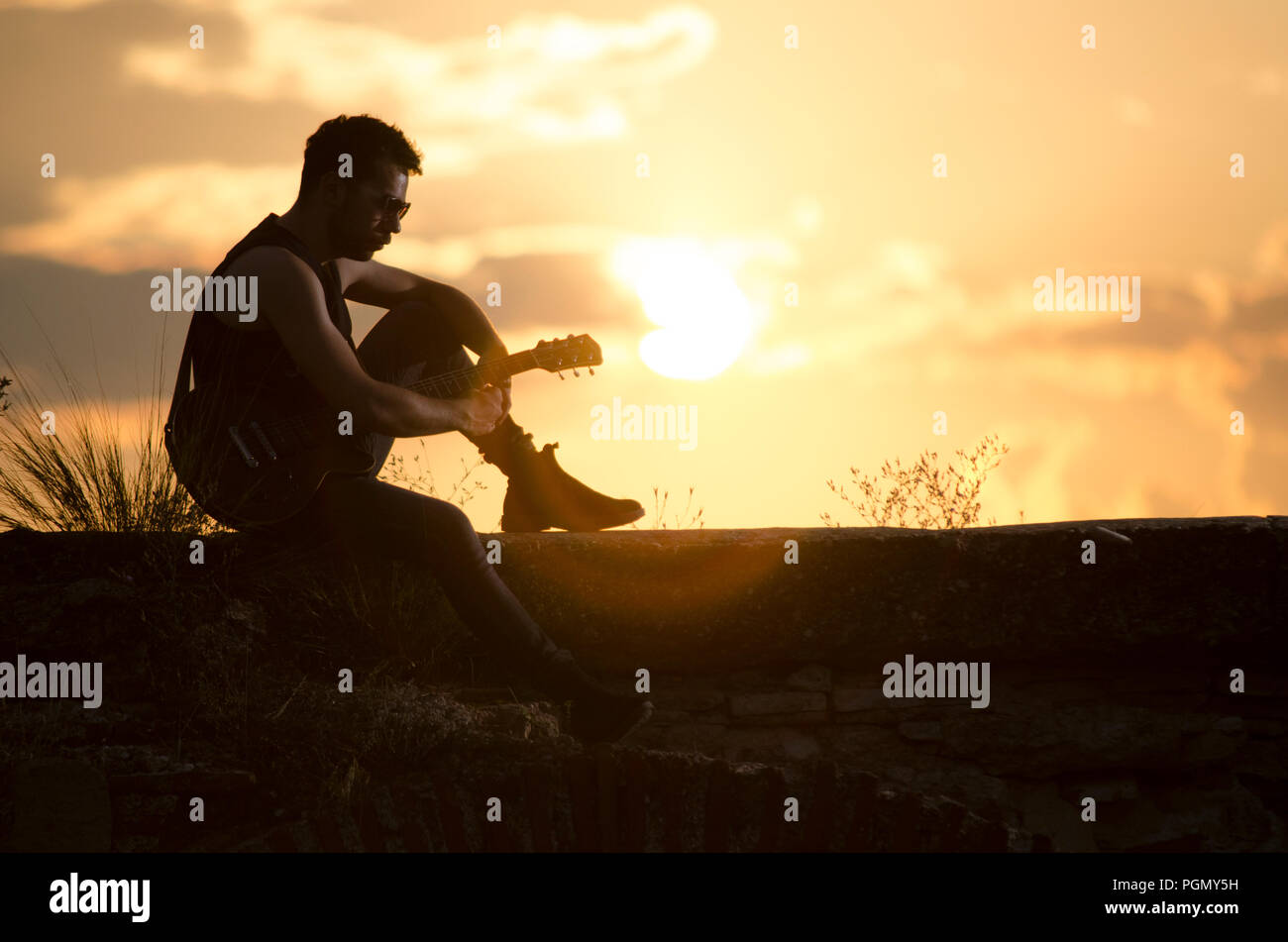 Man performs on electric guitar on old roman aqueduct during sunset ...