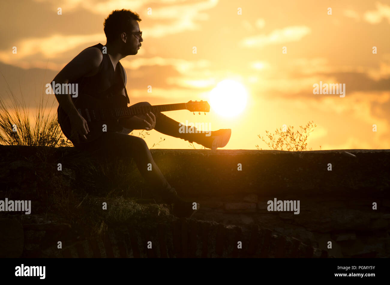 Man performs on electric guitar on old roman aqueduct during sunset ...