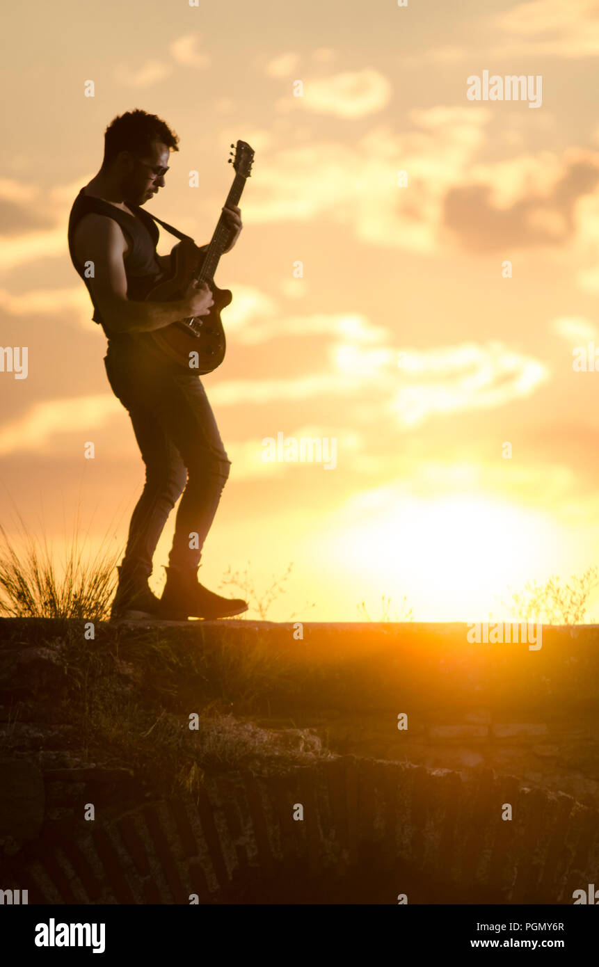 Man performs on electric guitar on old roman aqueduct during sunset ...