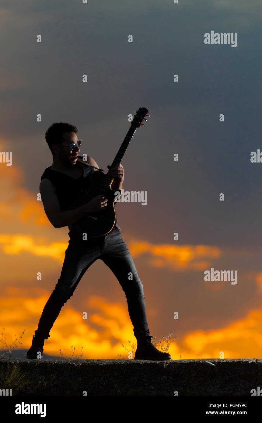 Man performs on electric guitar on old roman aqueduct during sunset ...