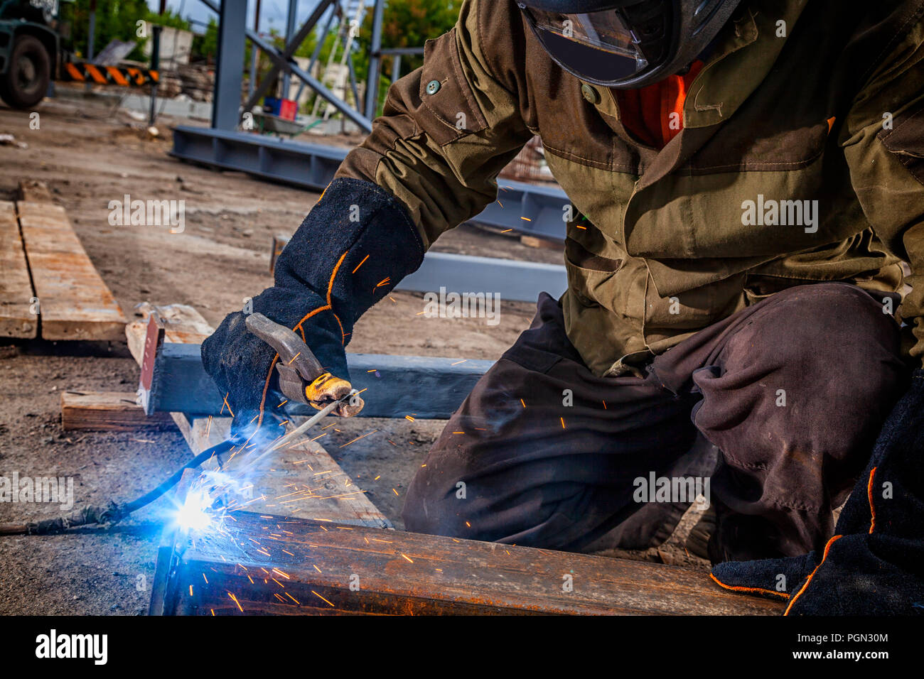 A strong man is a welder in brown uniform, welding mask and welders ...