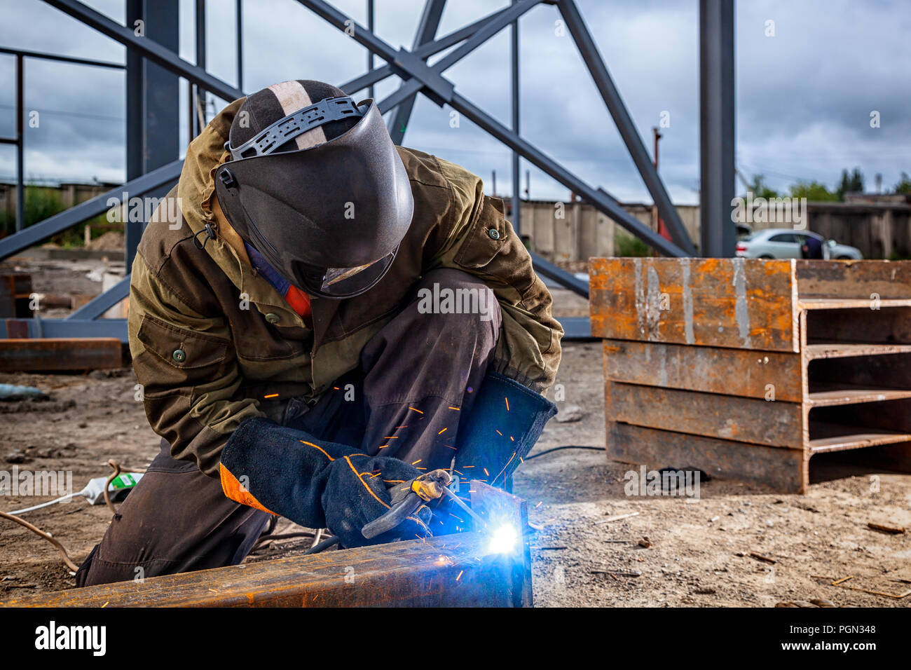 A young man welder in brown uniform, welding mask and welders leathers ...