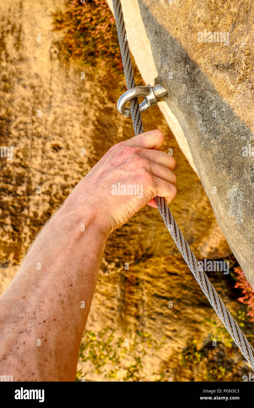 Male climber hand attaching via ferrata set to steel cable. Climbing up ...