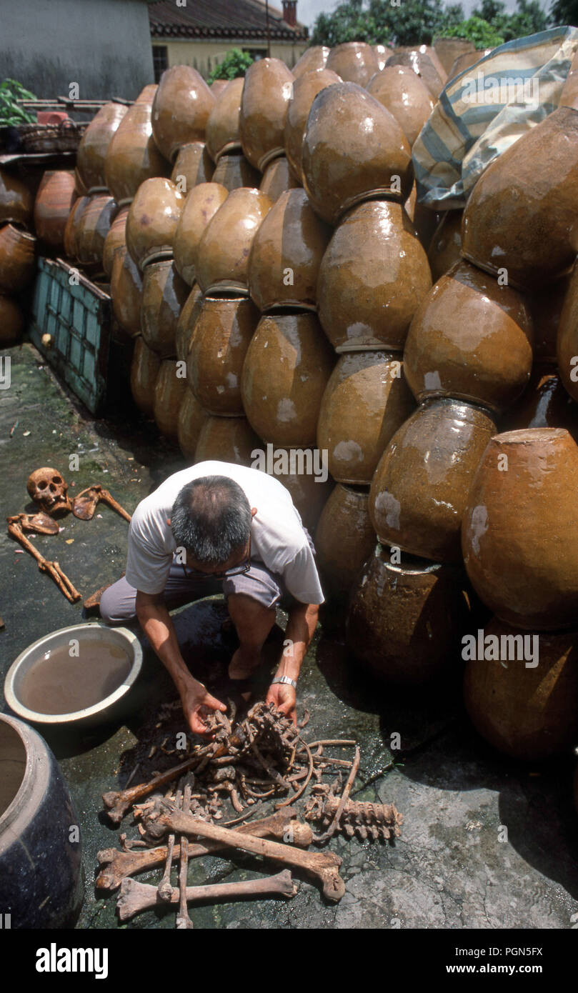 A Man removes bones from a earthenware earthenware jar and washes them ...