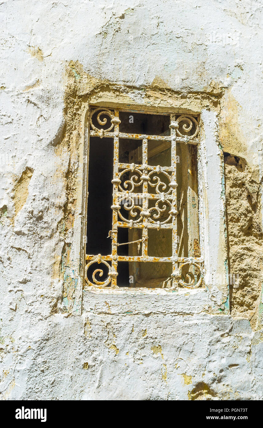 The old wall with crumbling plaster and rusty grill on tiny window ...