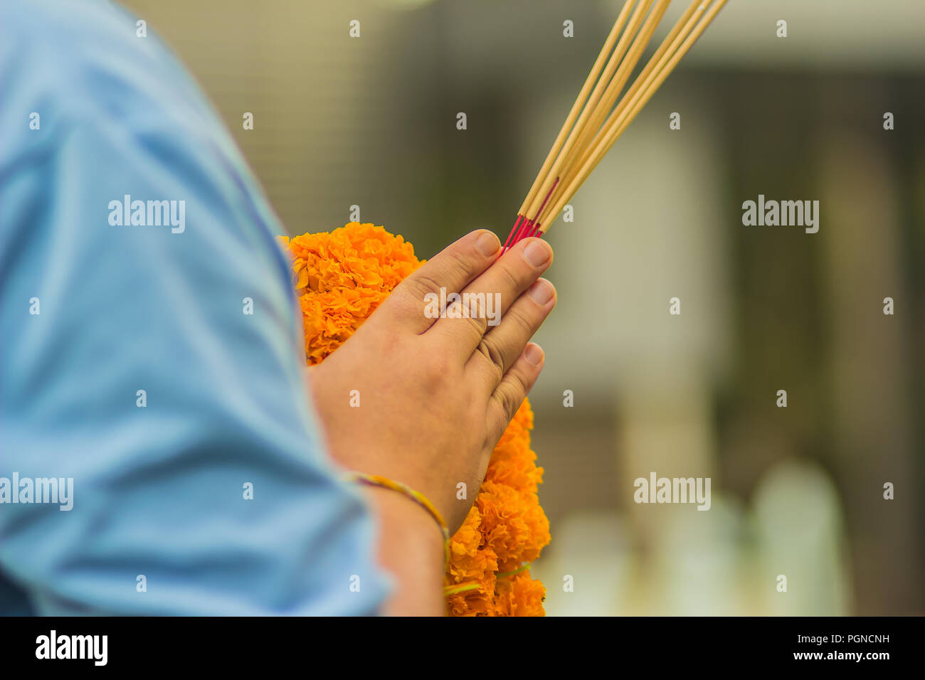 Close up people hands holding incense sticks and marigold, flower wheel ...